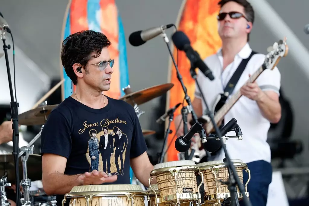 Feidhmíonn an t-aisteoir, léiritheoir agus óstach John Stamos (L) atá ainmnithe ag Gradam Emmy le The Beach Boys ag cleachtaí 2018 A Capitol Fourth ag US Capitol, West Lawn ar 3 Iúil, 2018 i Washington, DC.